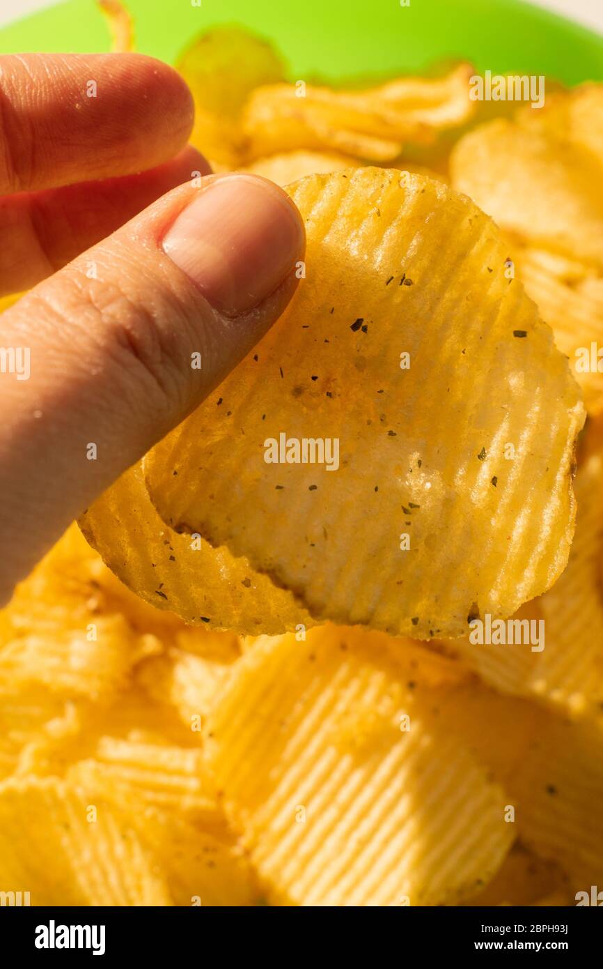 hand takes 1 chips from a plate with chips. corrugated potato chips ...