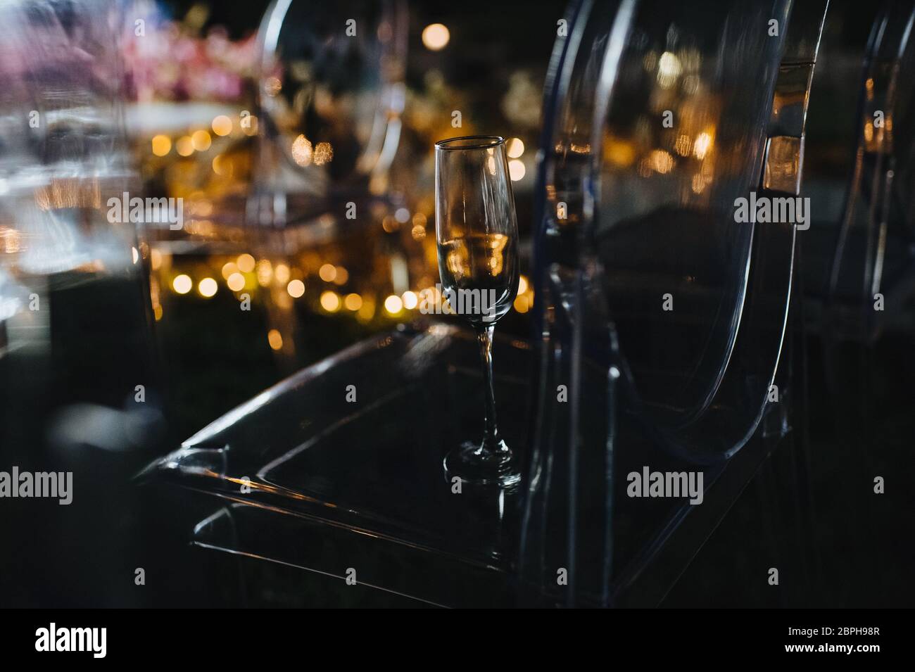 One champagne glass stands on a transparent glass chair. In the ...