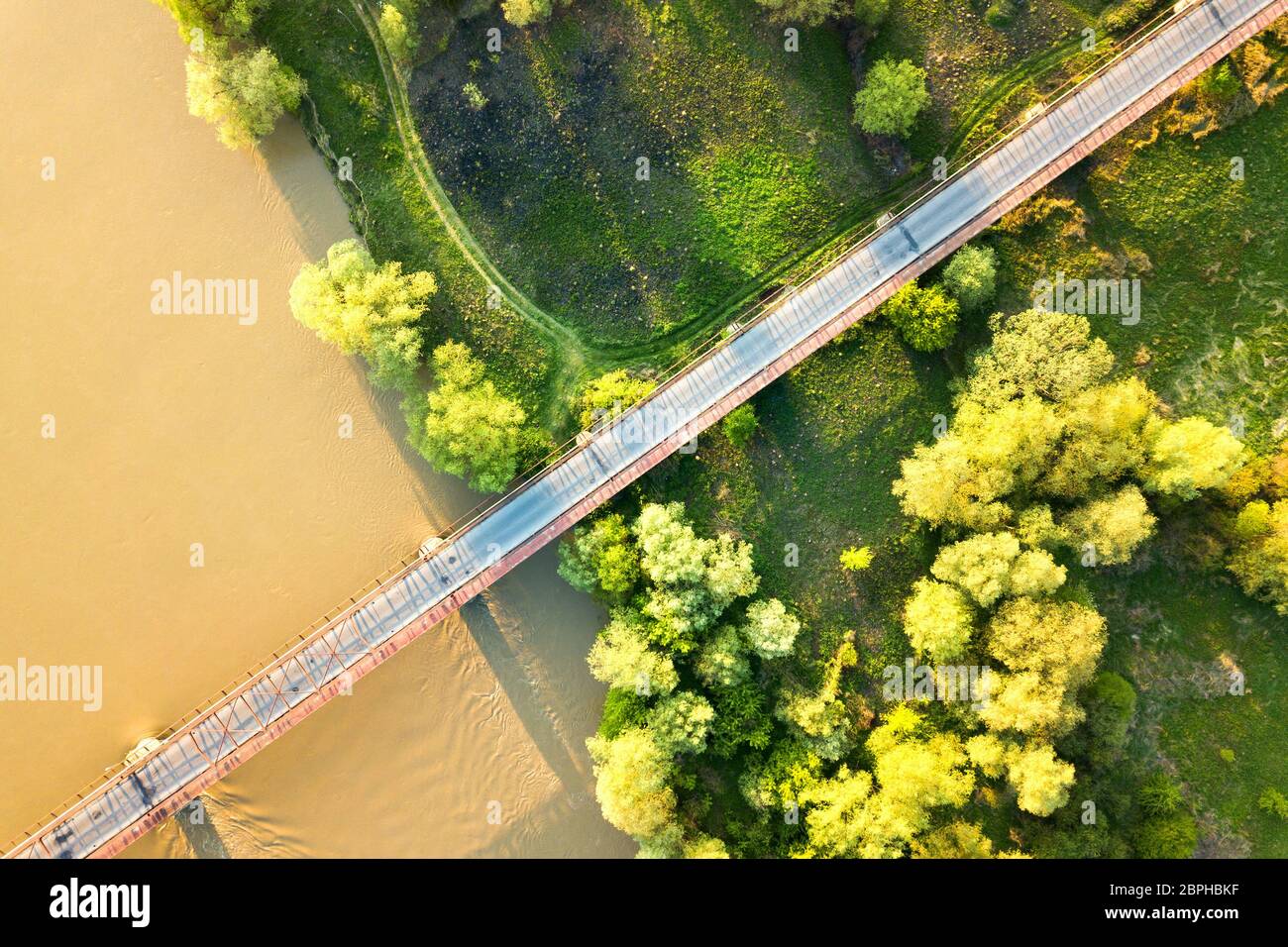 Aerial view of a narrow road bridge stretching over muddy wide river in ...