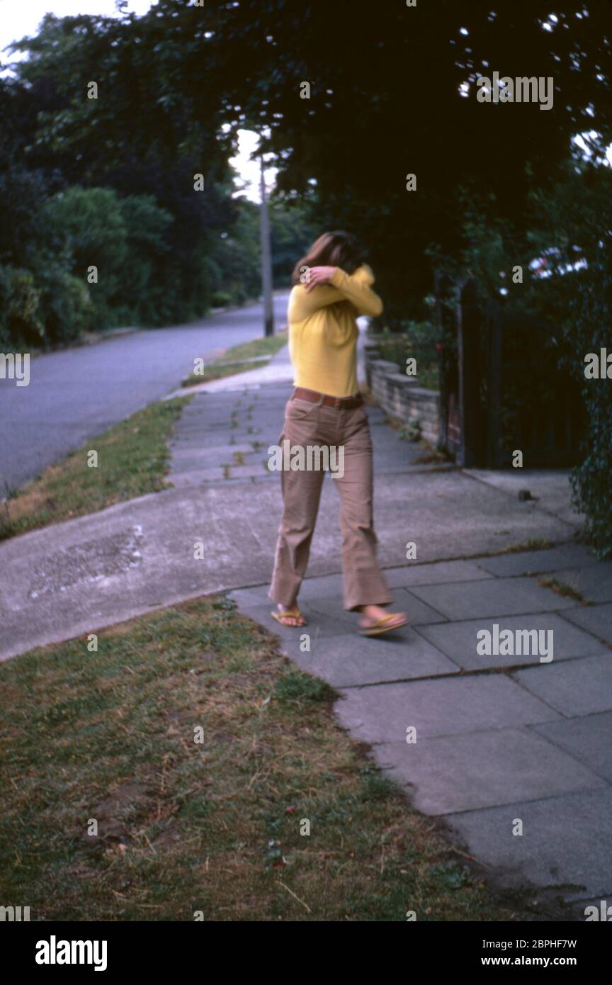 A young mum in her thirties walking down the road with her arms ...