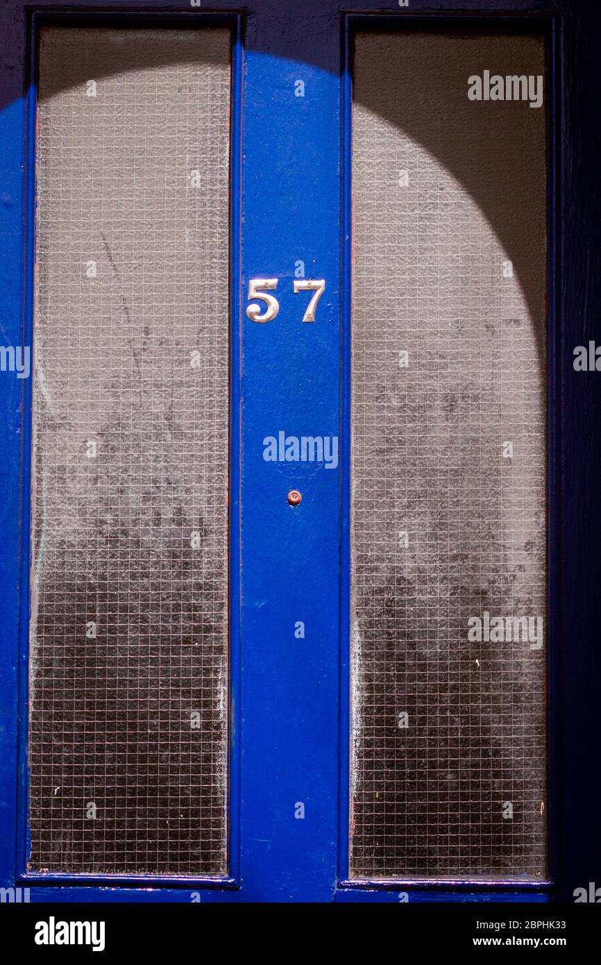 House number 57 on a royal blue wooden front door with dirty window ...