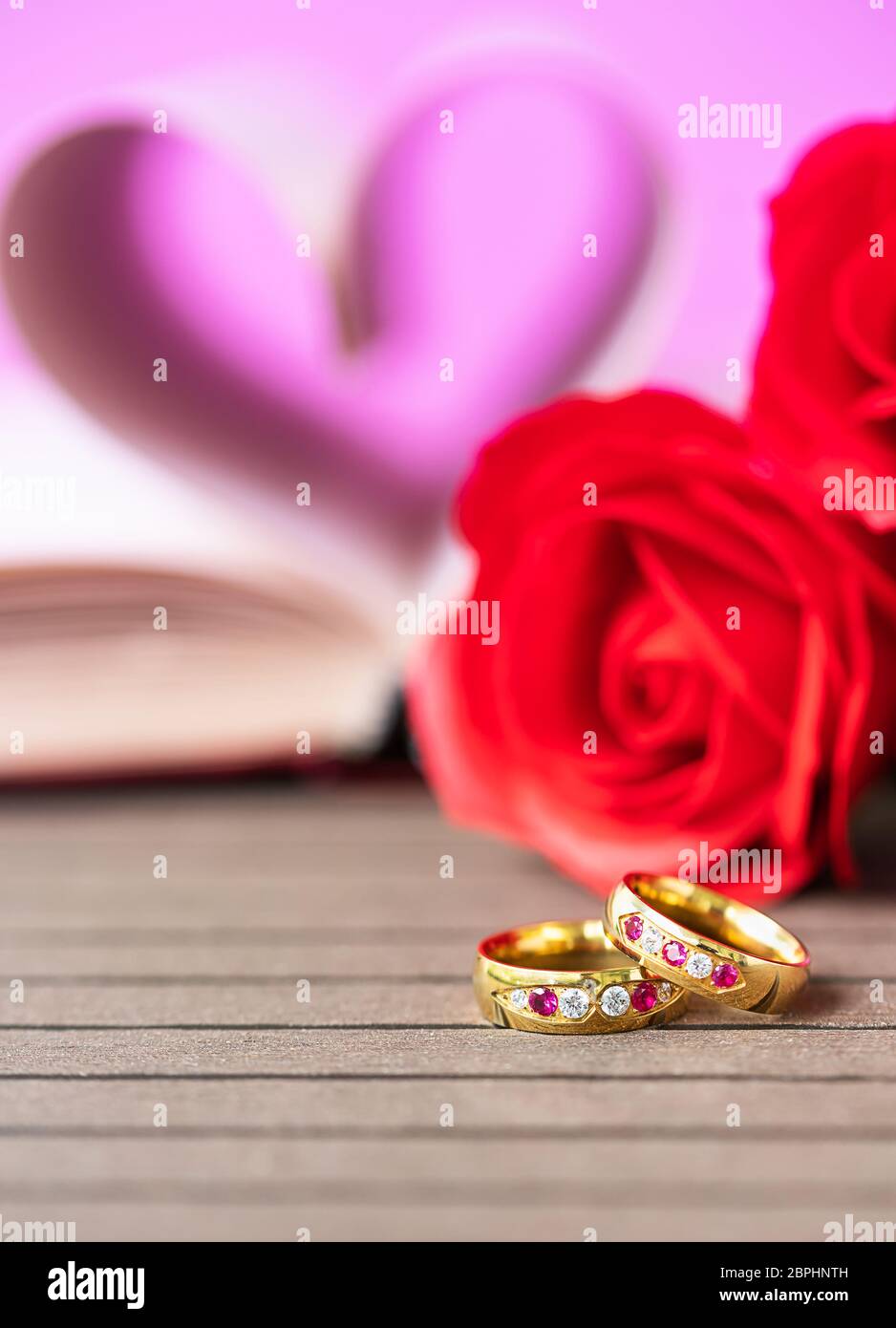 Pages of book curved into a heart shape with red rose and wedding ring ...