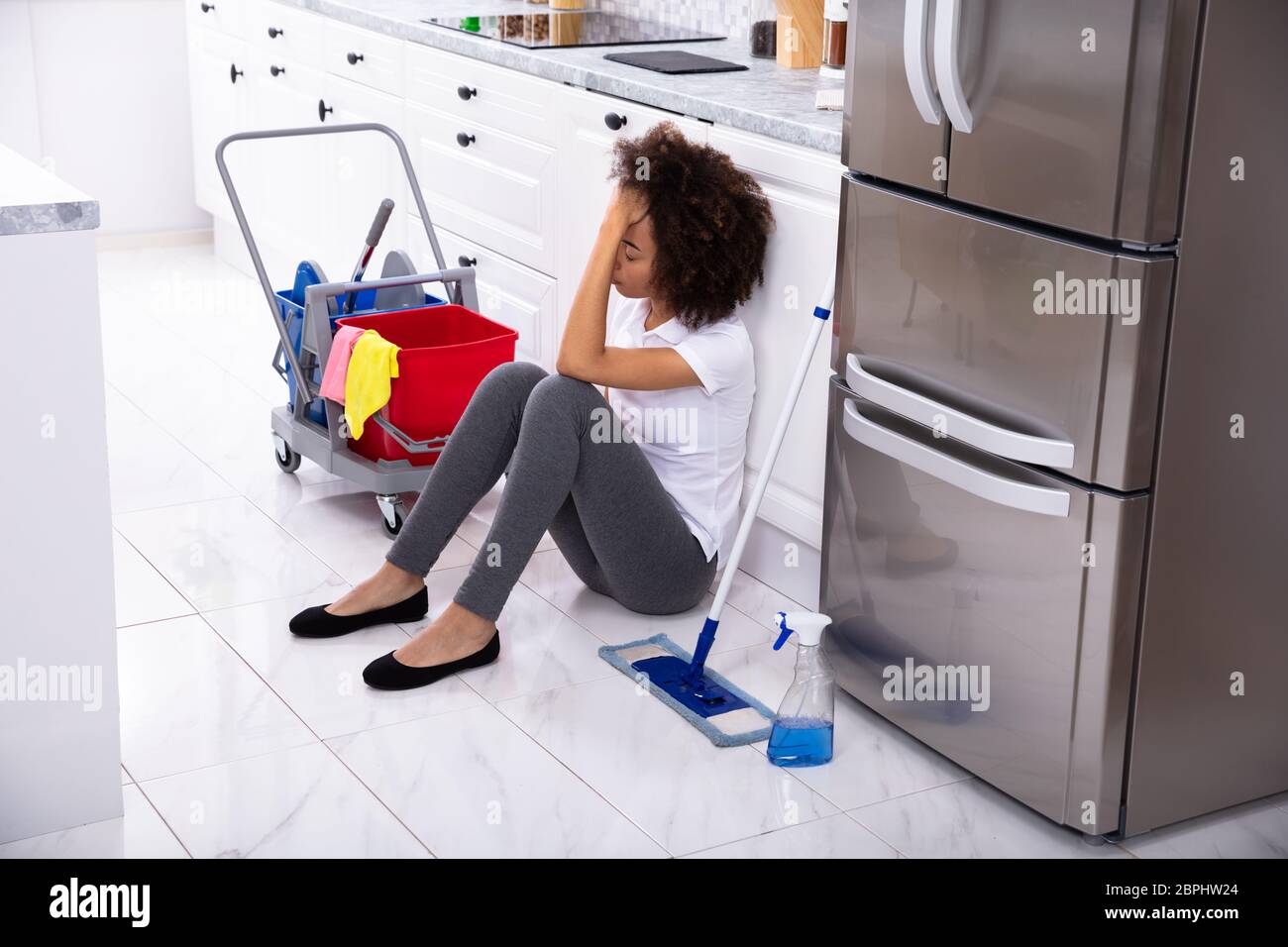 Exhausted African Young Woman Sitting On Floor In The Kitchen Stock ...