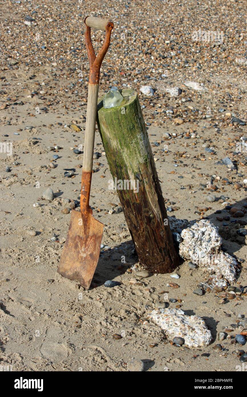 Old wooden handled spade leaning against a half buried breakwater on a ...