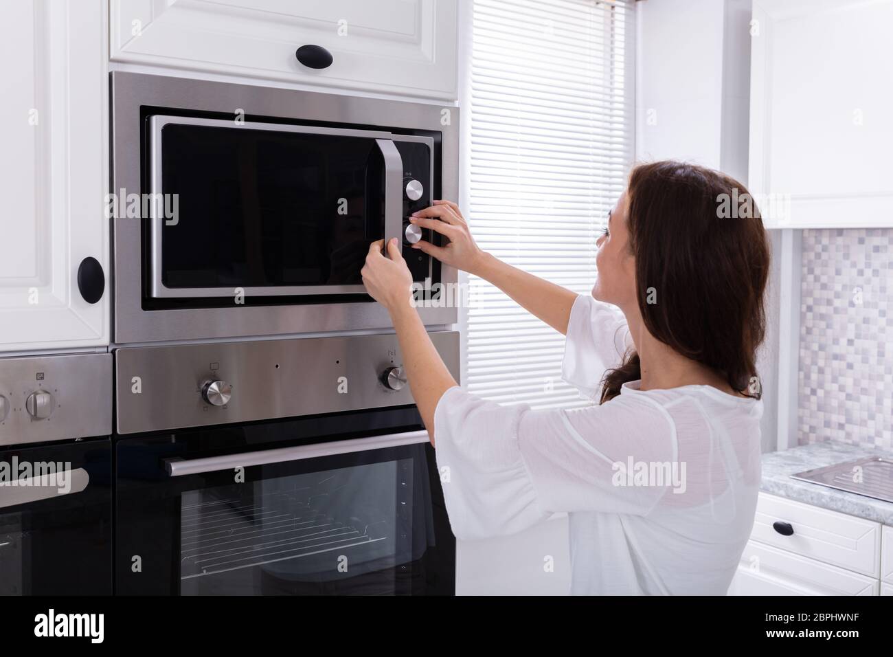 Side View Of A Young Woman Using Microwave Oven In Kitchen Stock Photo ...