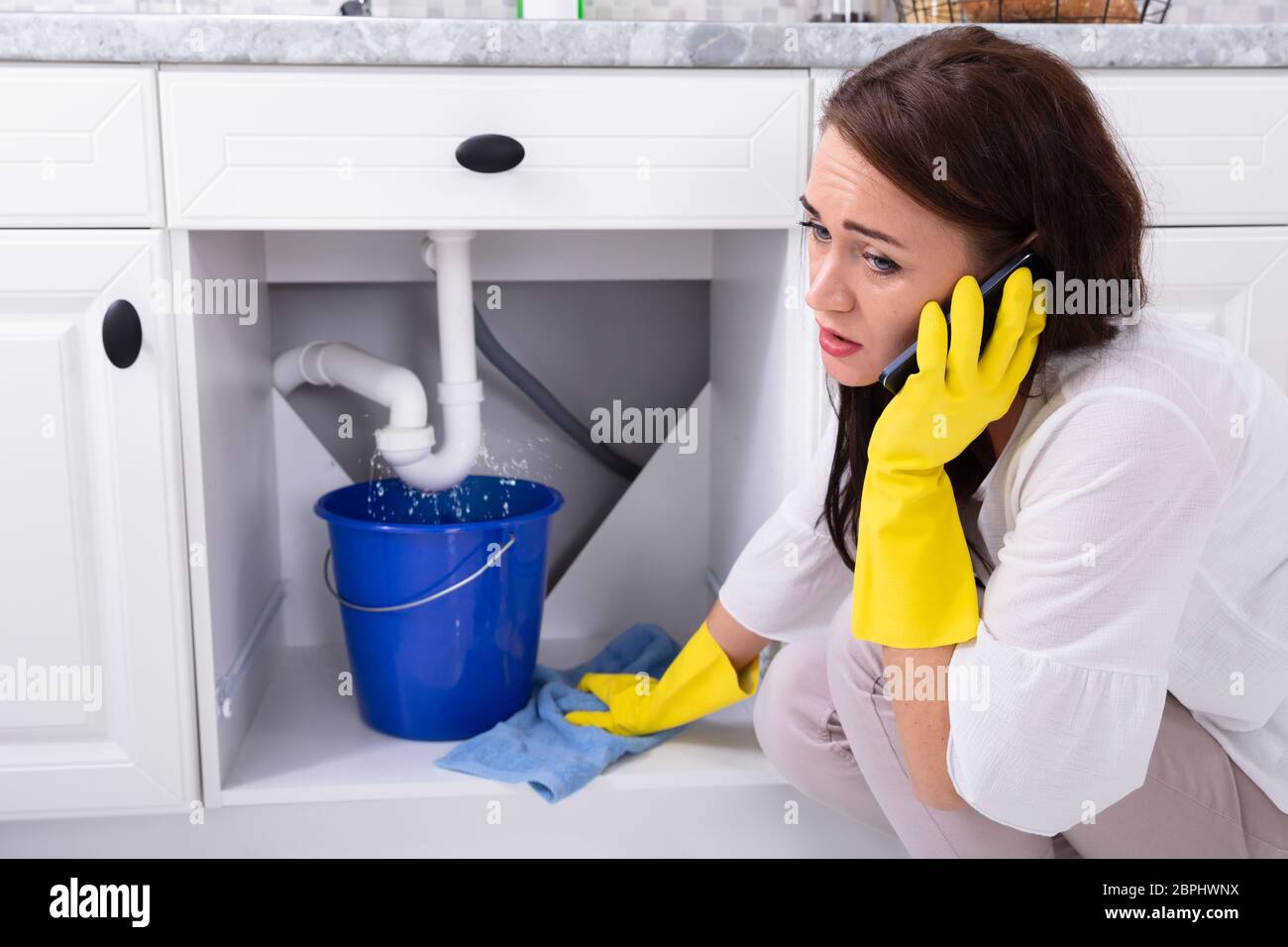 Sad Young Woman Calling Plumber In Front Of Water Leaking From Sink ...
