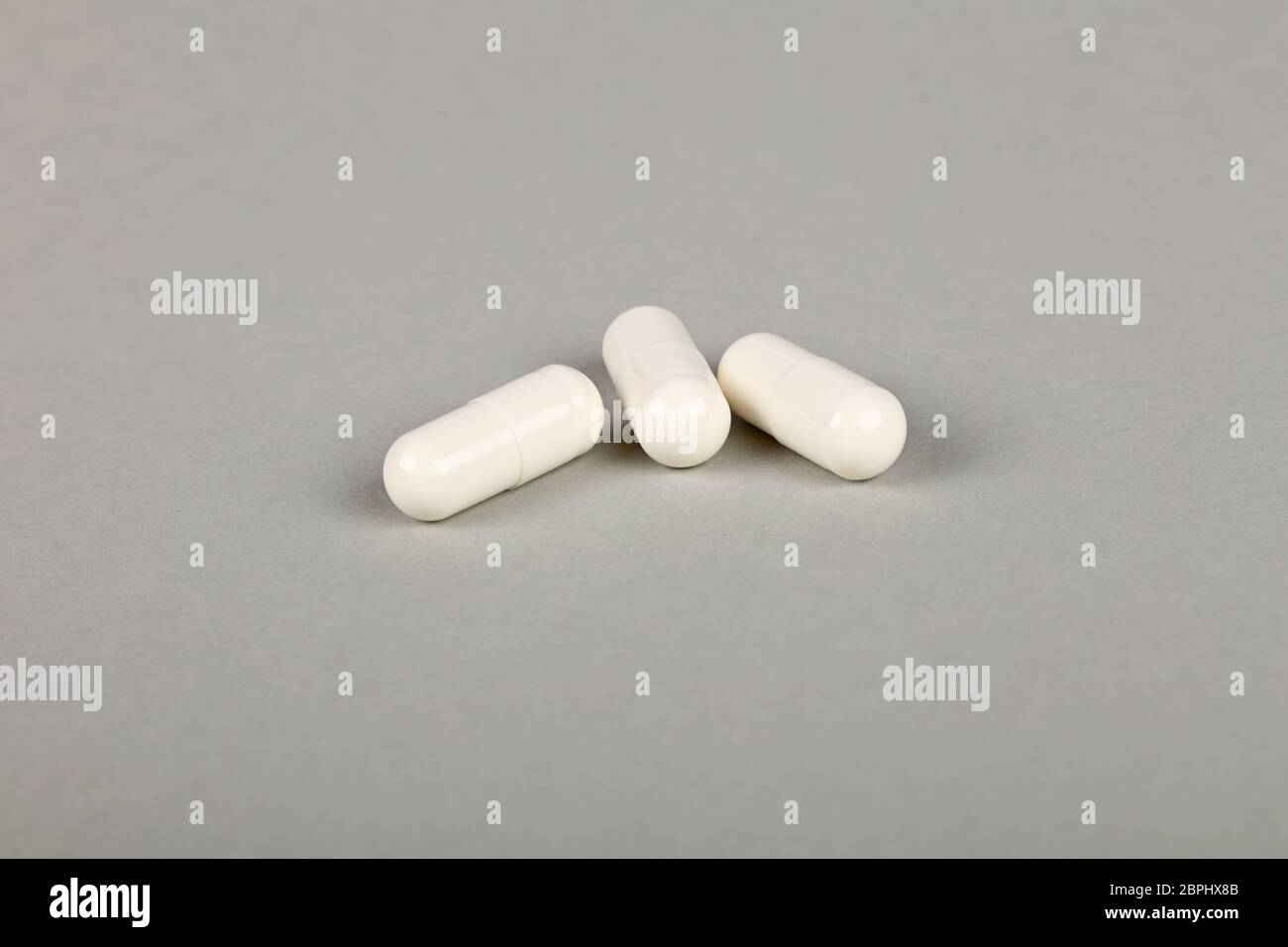 Close up three white gel cap pills of medicine over grey background ...