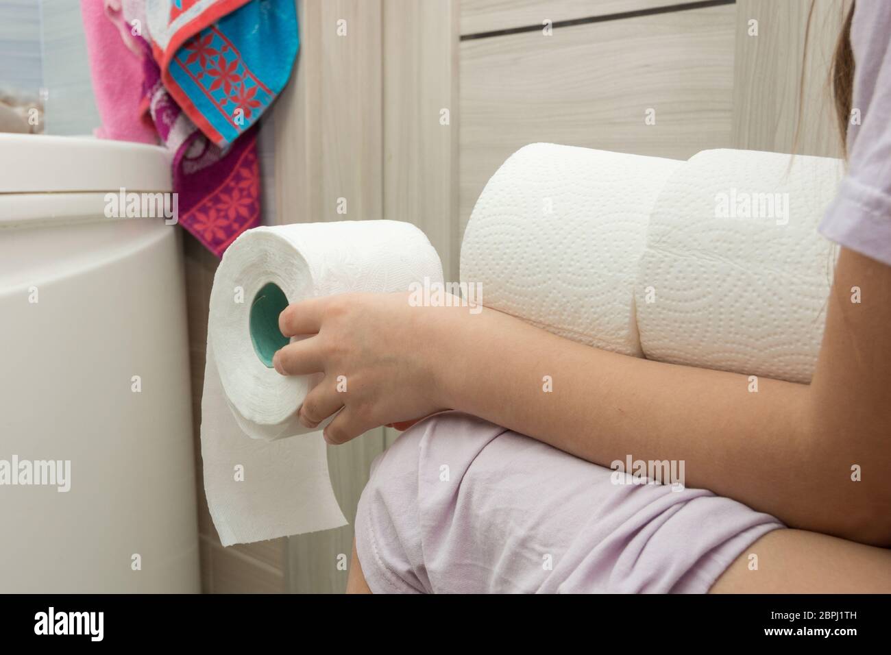 The girl is sitting on the toilet and holding a few rolls of toilet ...