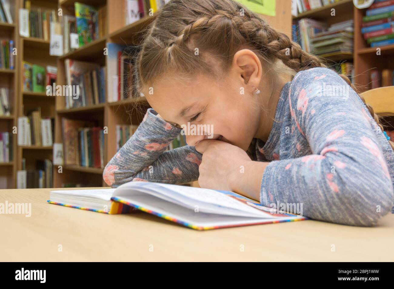 Girl laughing while reading a book in the library Stock Photo - Alamy