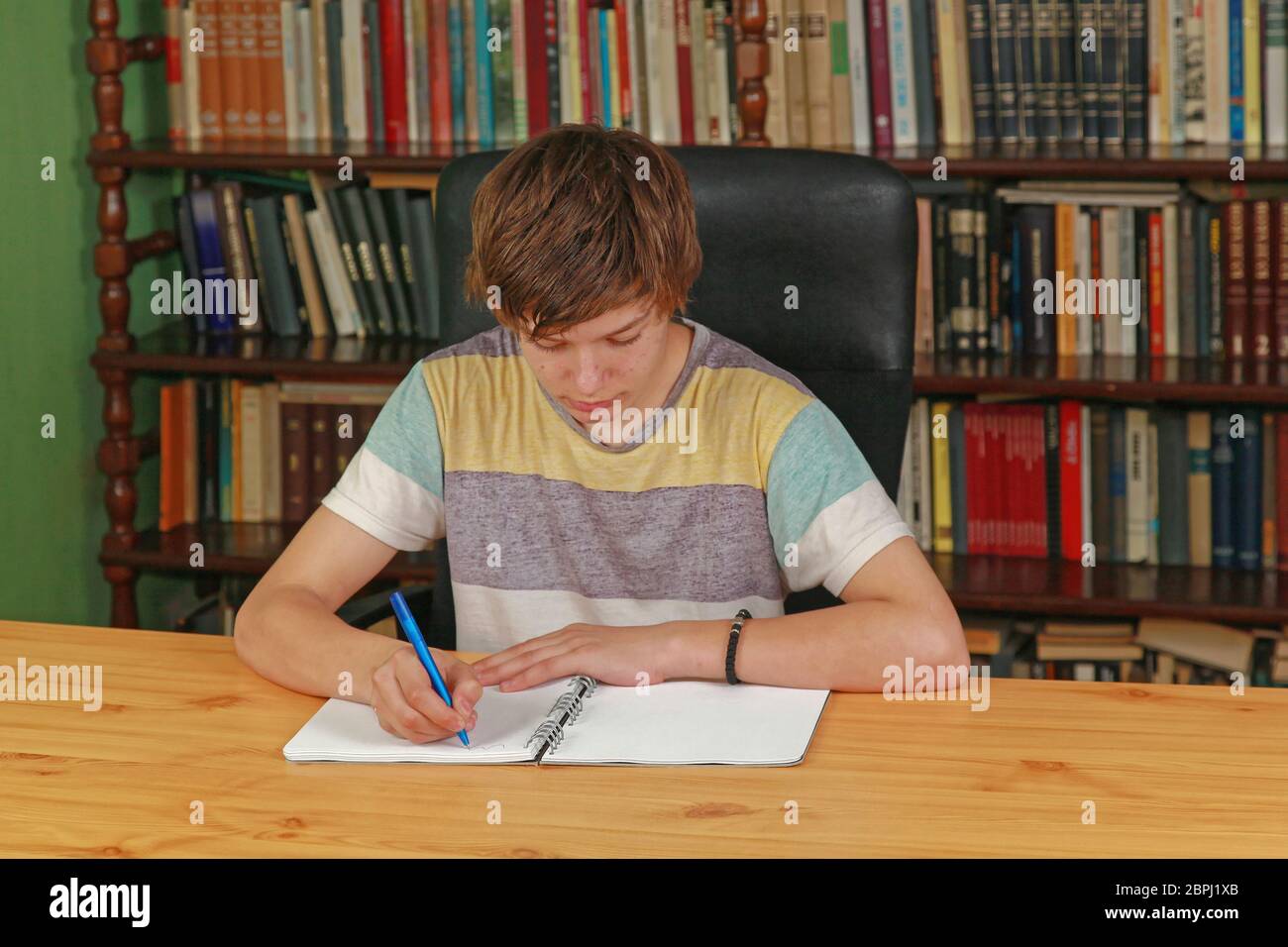 Teenage Boy Writing at Desk in School Library Stock Photo - Alamy