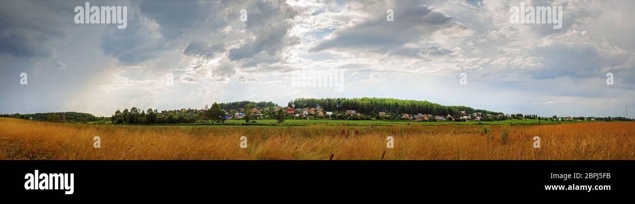 Panoramic rural landscape. Sky with clouds, dried grass field, houses ...