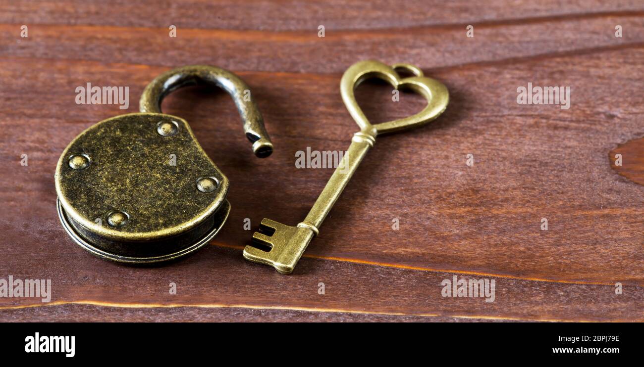 Gold vintage heart key and unlocked padlock on wooden background. Sweet ...