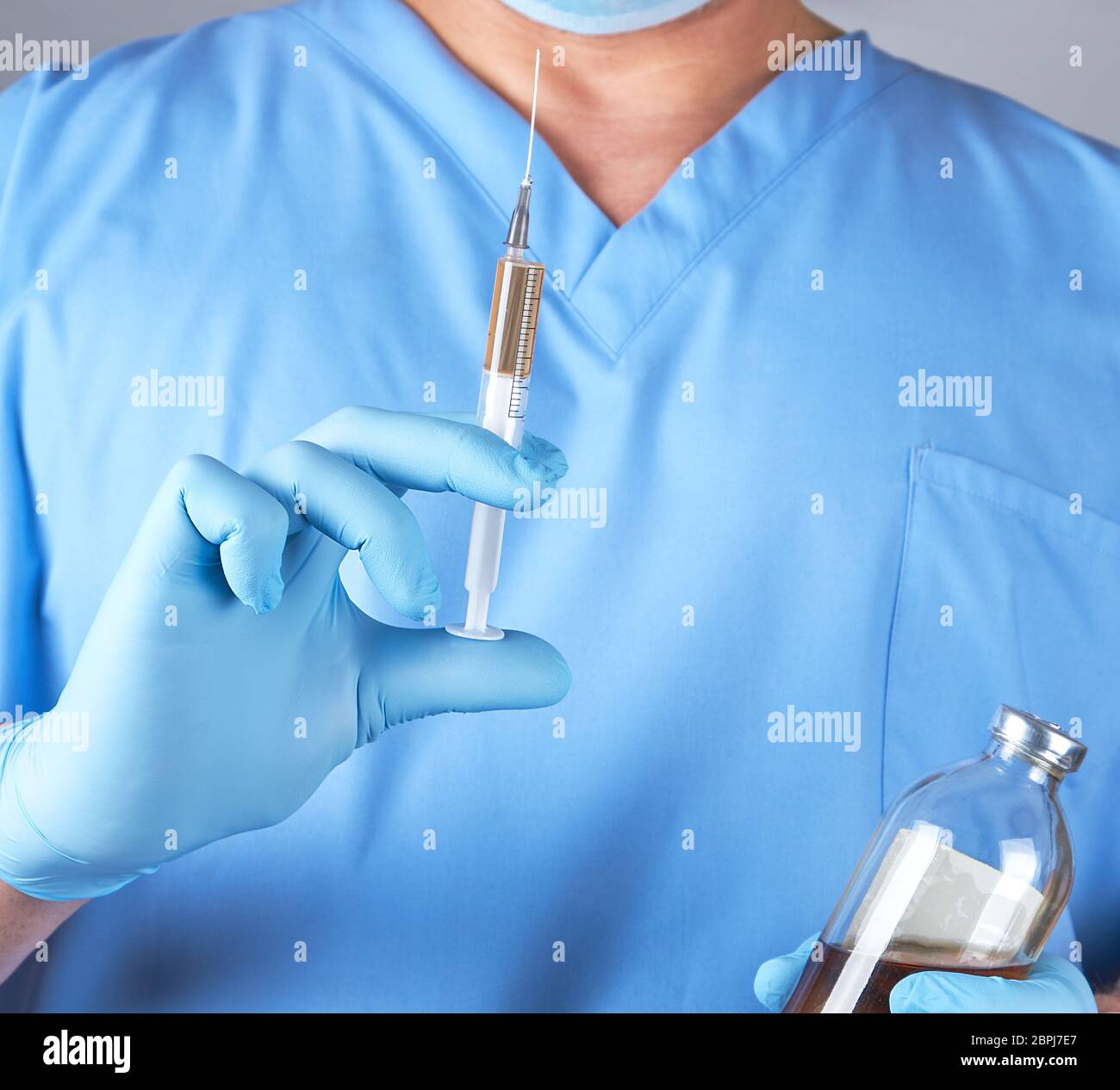 male doctor in blue uniform holding a syringe with red liquid for ...