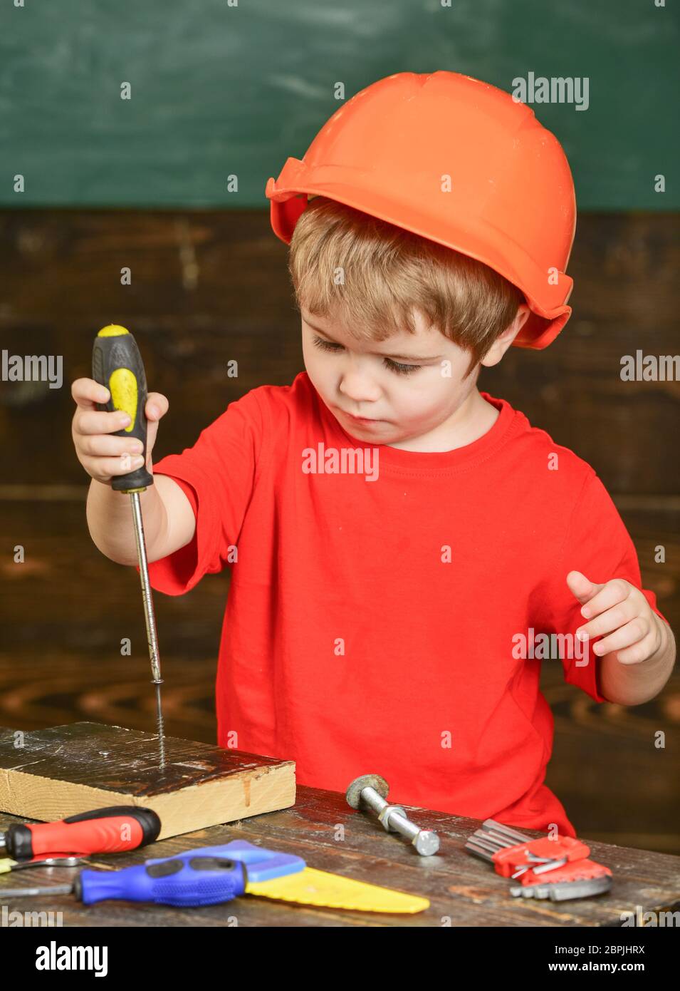 Kid boy holds screwdriver tool. Toddler on busy face plays with ...