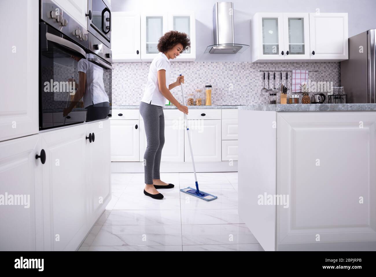 Side View Of A Smiling Female Janitor Cleaning White Floor With Mop In ...