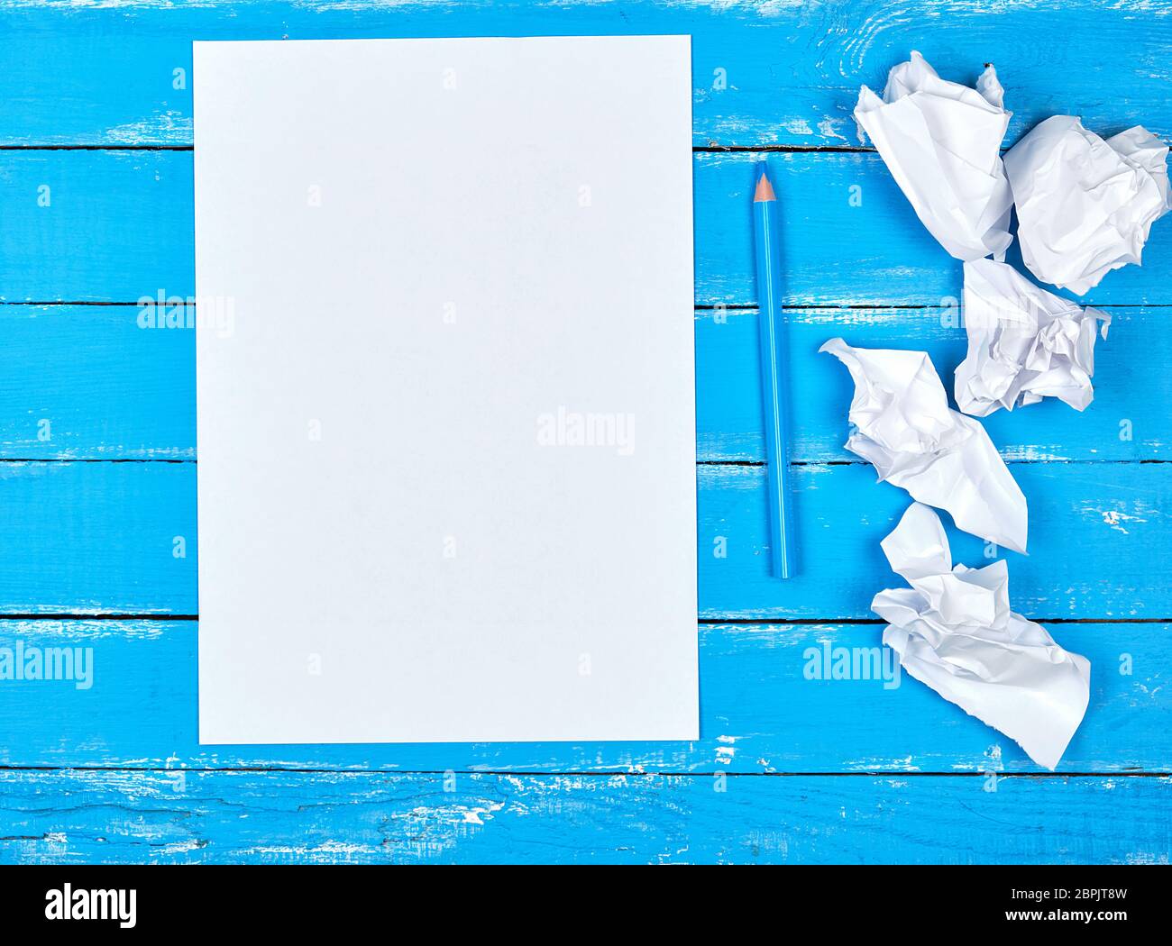 blank white rectangular sheet of paper and crumpled pieces of paper on a blue wooden shabby ...