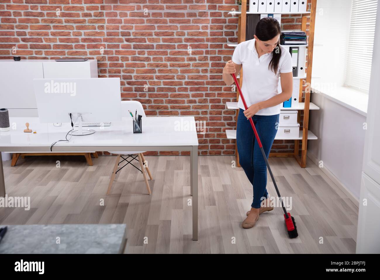 Happy Young Female Janitor Cleaning Floor With Broom In Office Stock ...