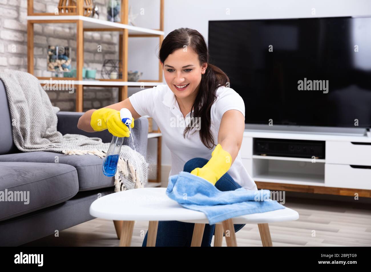 Smiling Female Janitor Cleaning Table With Spray Bottle At Home Stock ...