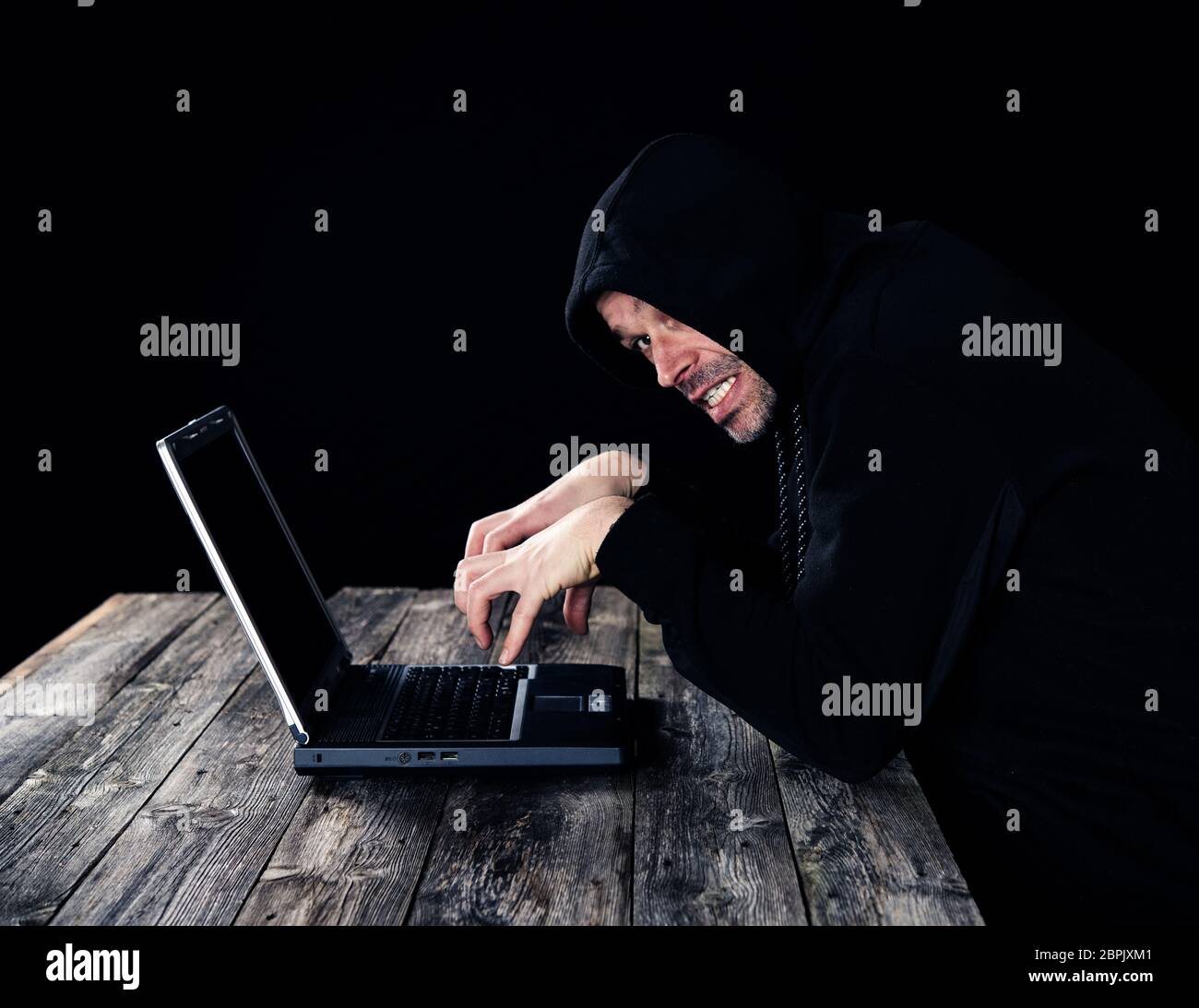 hacker in black hoody with laptop in front of black background Stock ...