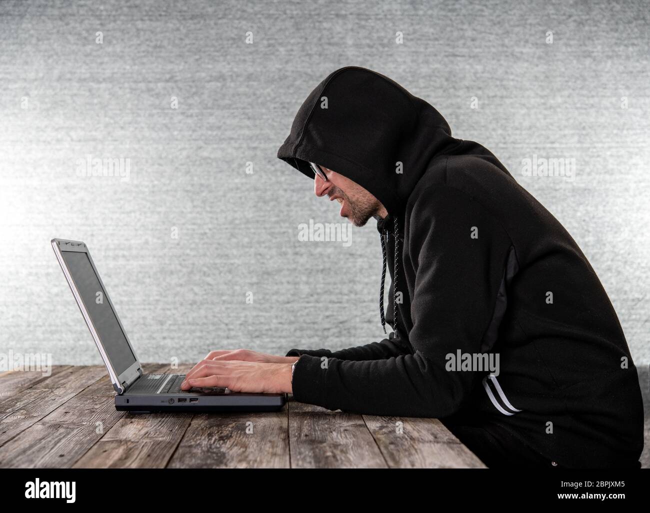 hacker in black hoody with laptop in front of gray background Stock ...
