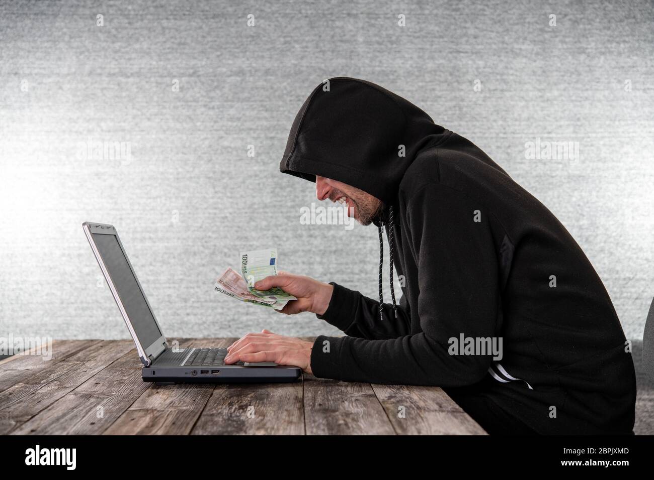 hacker in black hoody with laptop and euro notes in front of gray ...