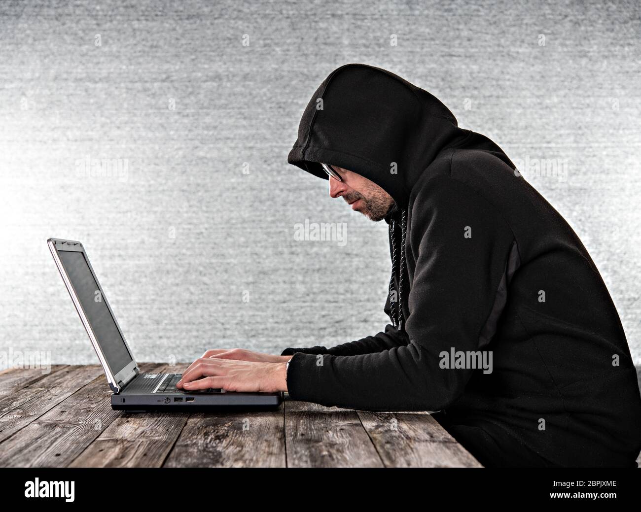 hacker in black hoody with laptop in front of gray background Stock ...