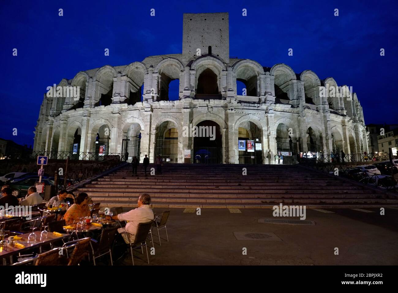 The night view Arles Amphitheatre and medieval tower with outdoor cafe ...