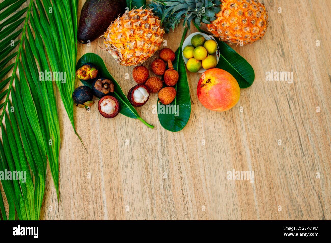 Flat lay Mix of Exotic fruits and palm leaf on a brown background ...