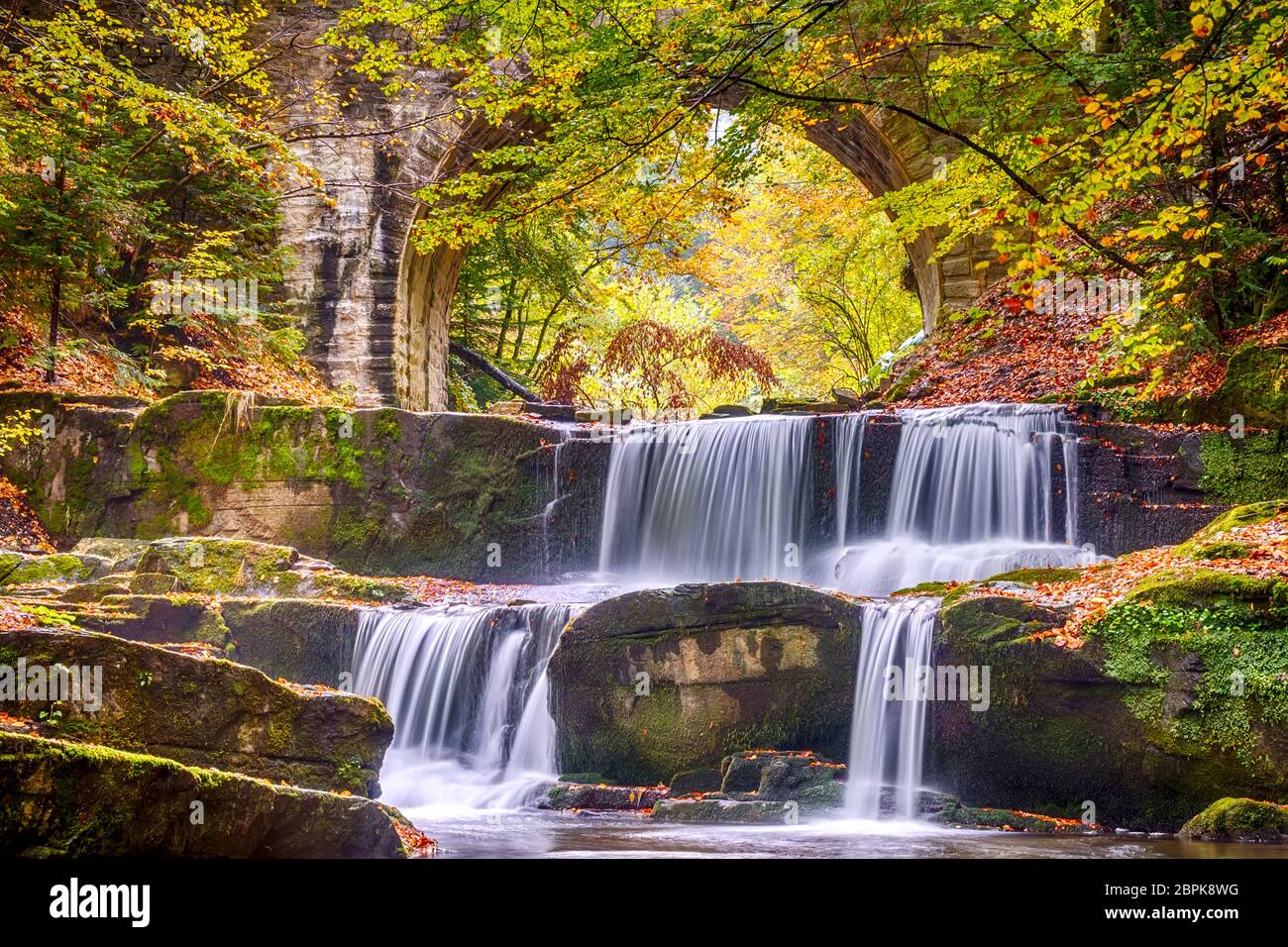 Autumn day in the sunny forest. Old stone bridge. Small river and several natural waterfalls ...