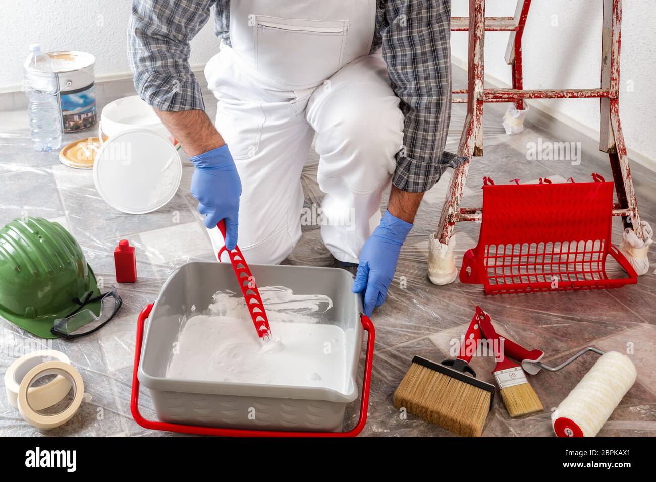 Caucasian house painter worker in white work overalls, mixes the paint ...