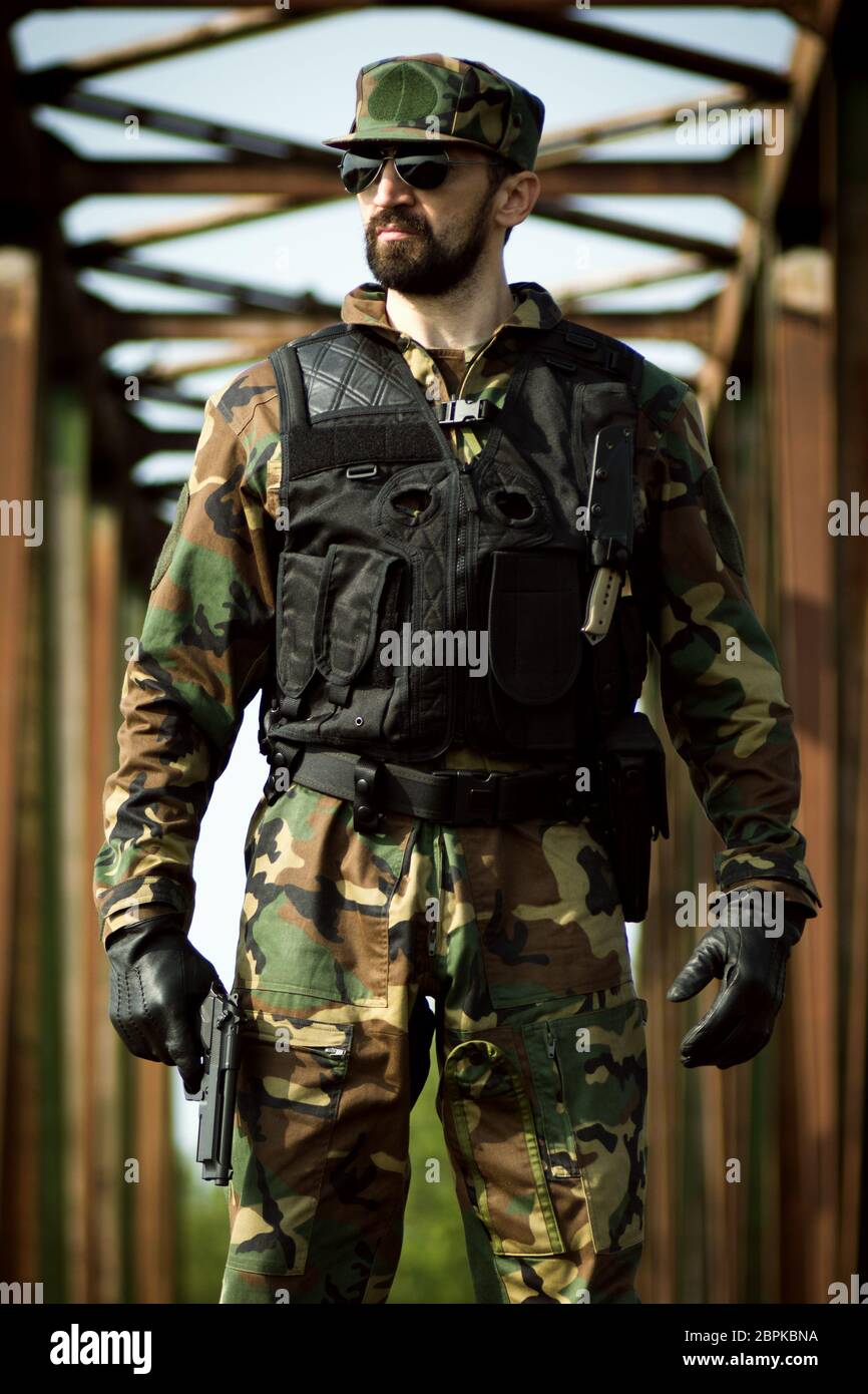 The confident bearded military man is standing with gun in hand ...