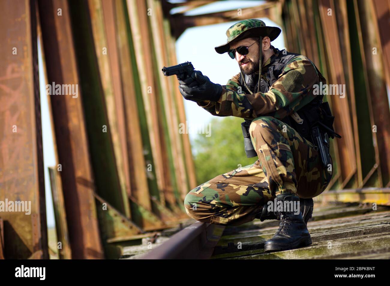 Army soldier in military uniform is aiming with pistol on railway ...