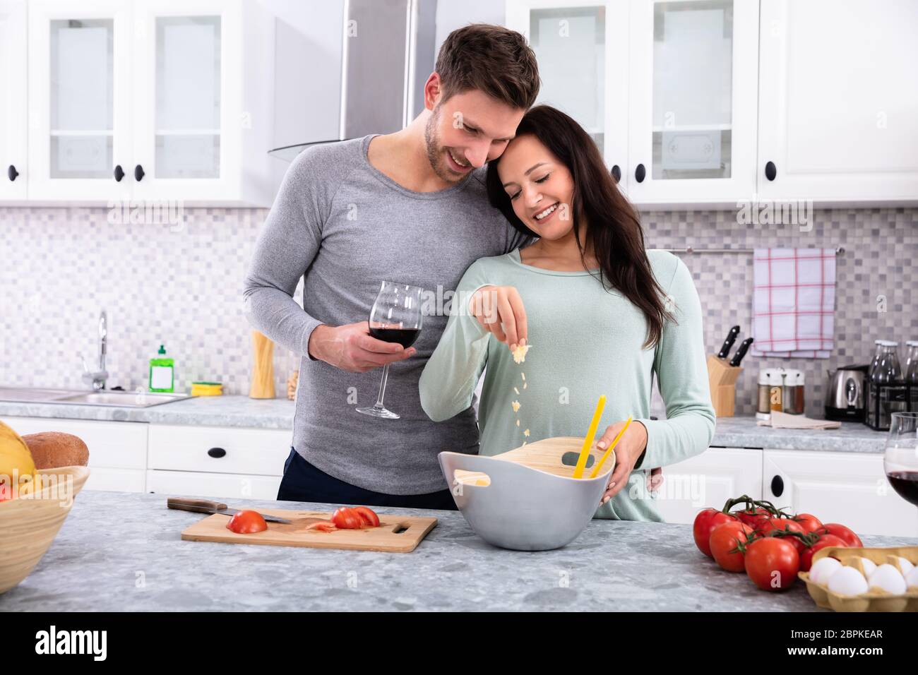 Smiling Wife Sprinkling Butter With Her Husband Standing In Kitchen ...