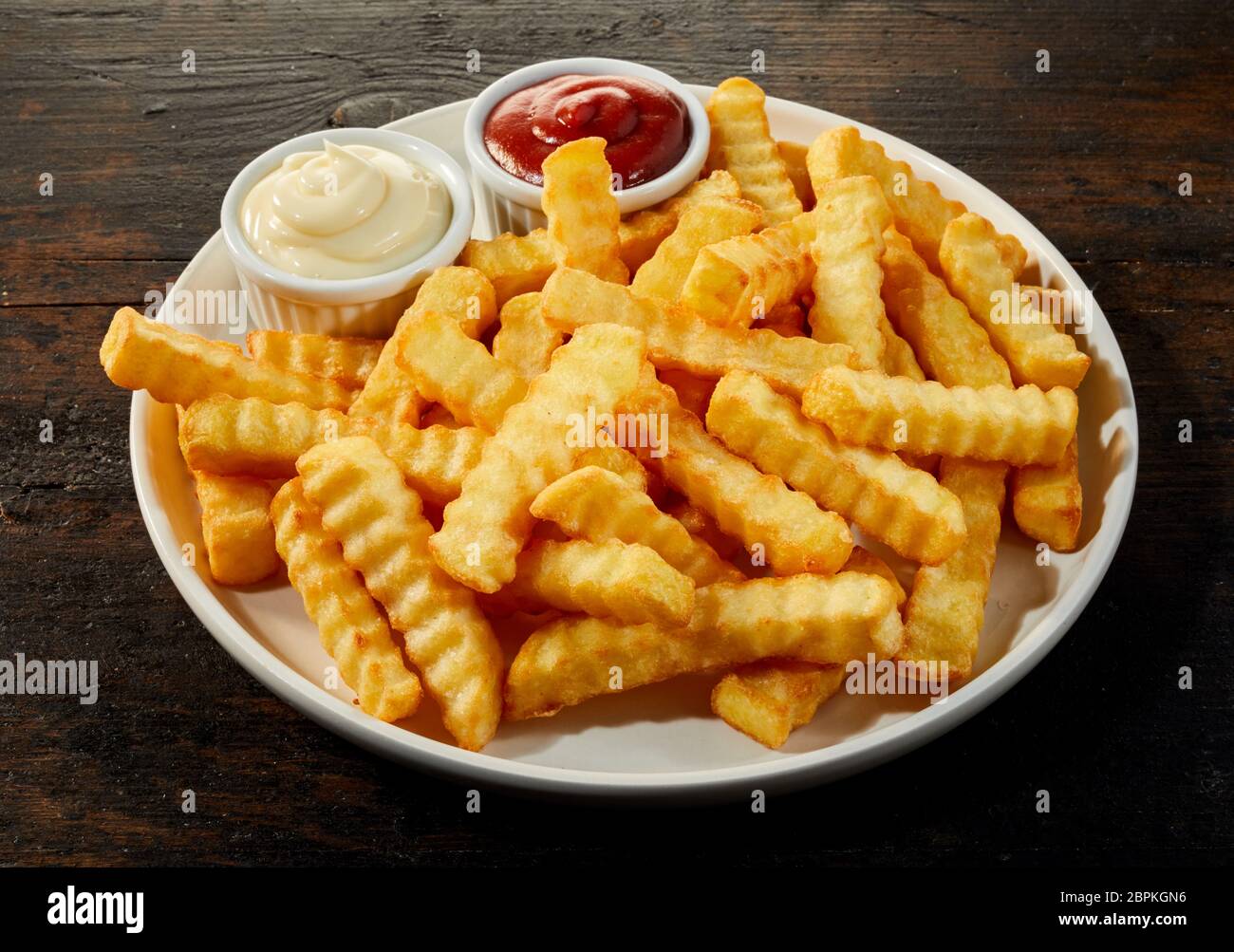 Plate of crinkle cut crisp golden French fries with mustard, mayonnaise ...