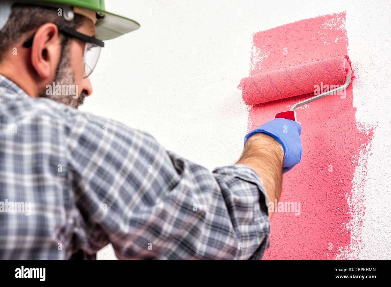 Caucasian house painter worker with helmet and goggles, with the roller ...