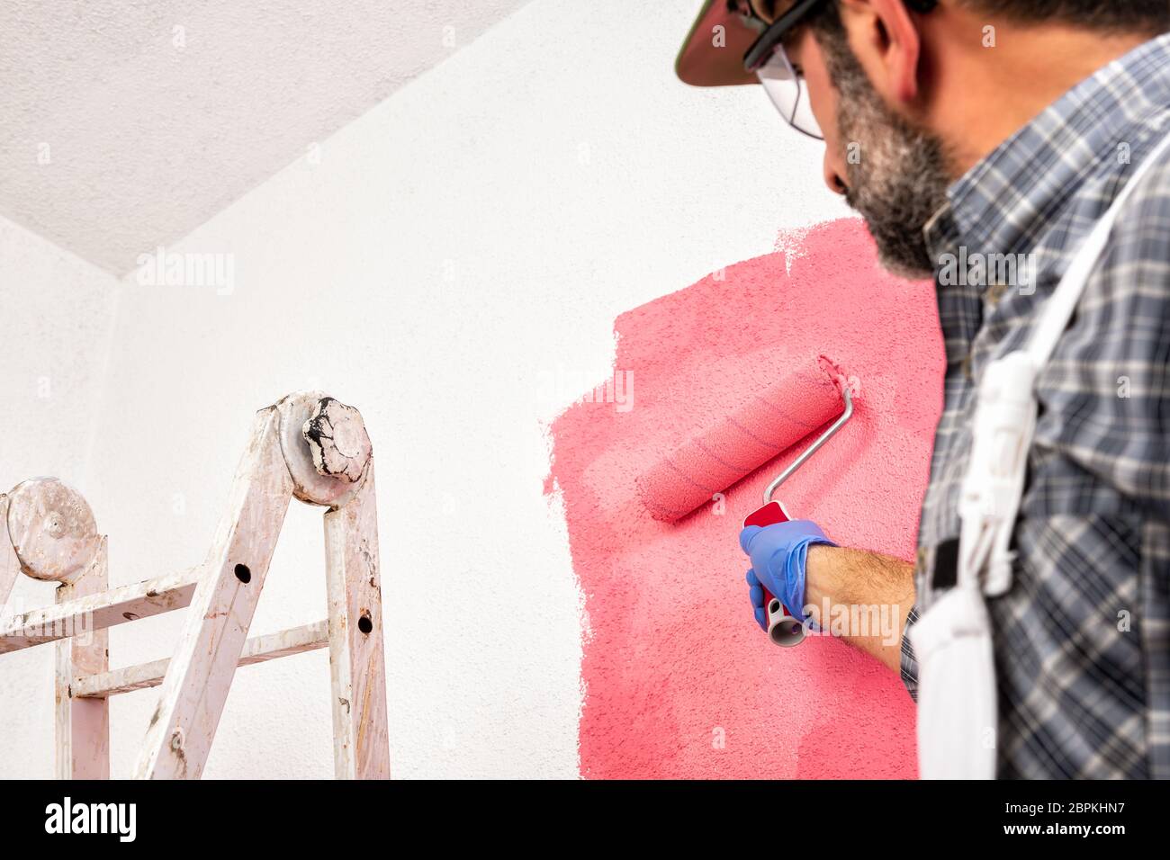 Caucasian house painter worker in white work overalls, with the roller ...