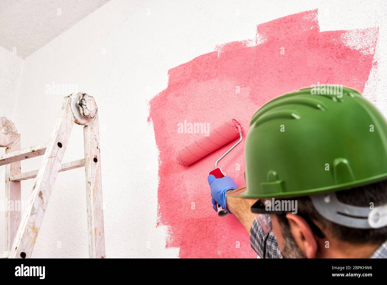 Caucasian house painter worker with helmet and goggles, with the roller ...