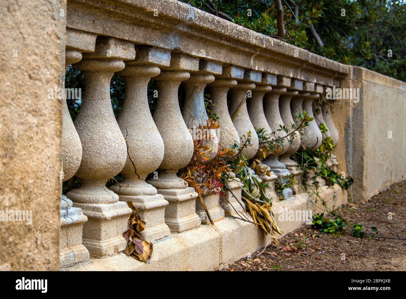 Old balusters made of stone enclosing the garden. Ivy branches pass ...