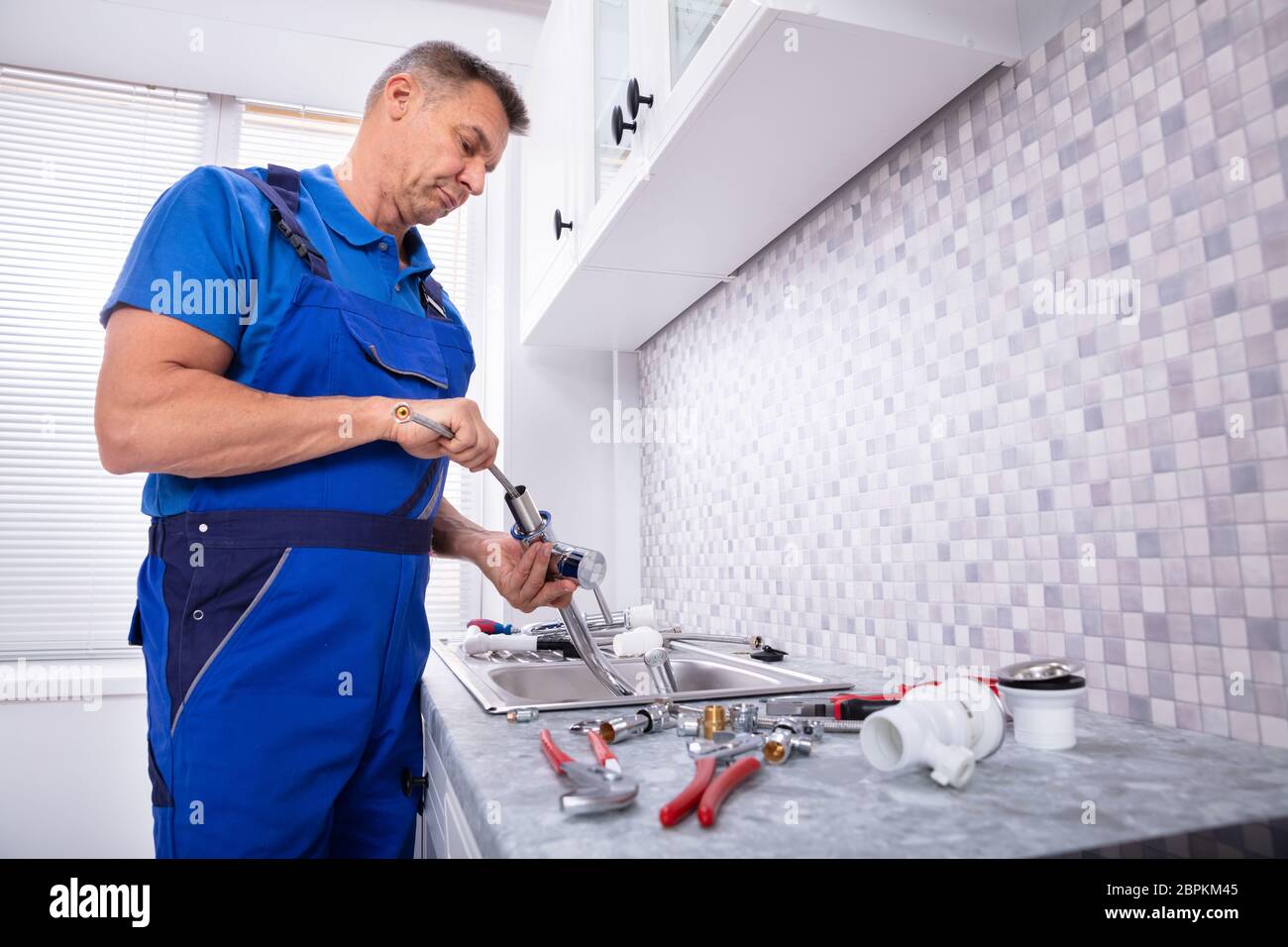 Side View Of A Plumber Fixing Water Tap In Kitchen Stock Photo - Alamy