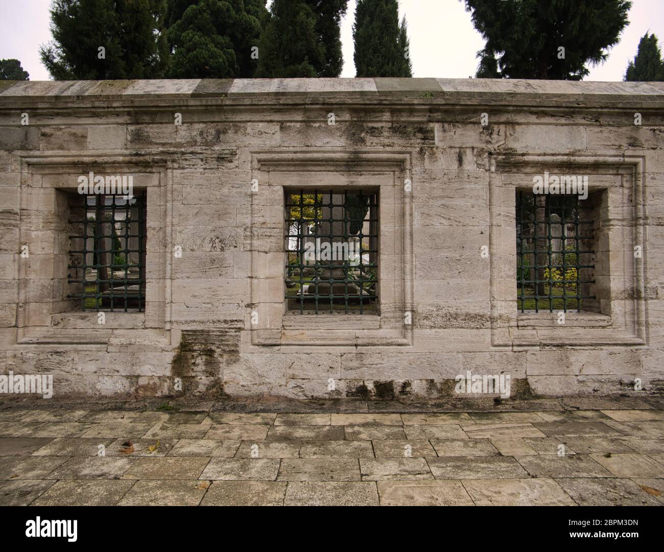 Detail of a stone wall with open lattice windows in front of a cemetery ...