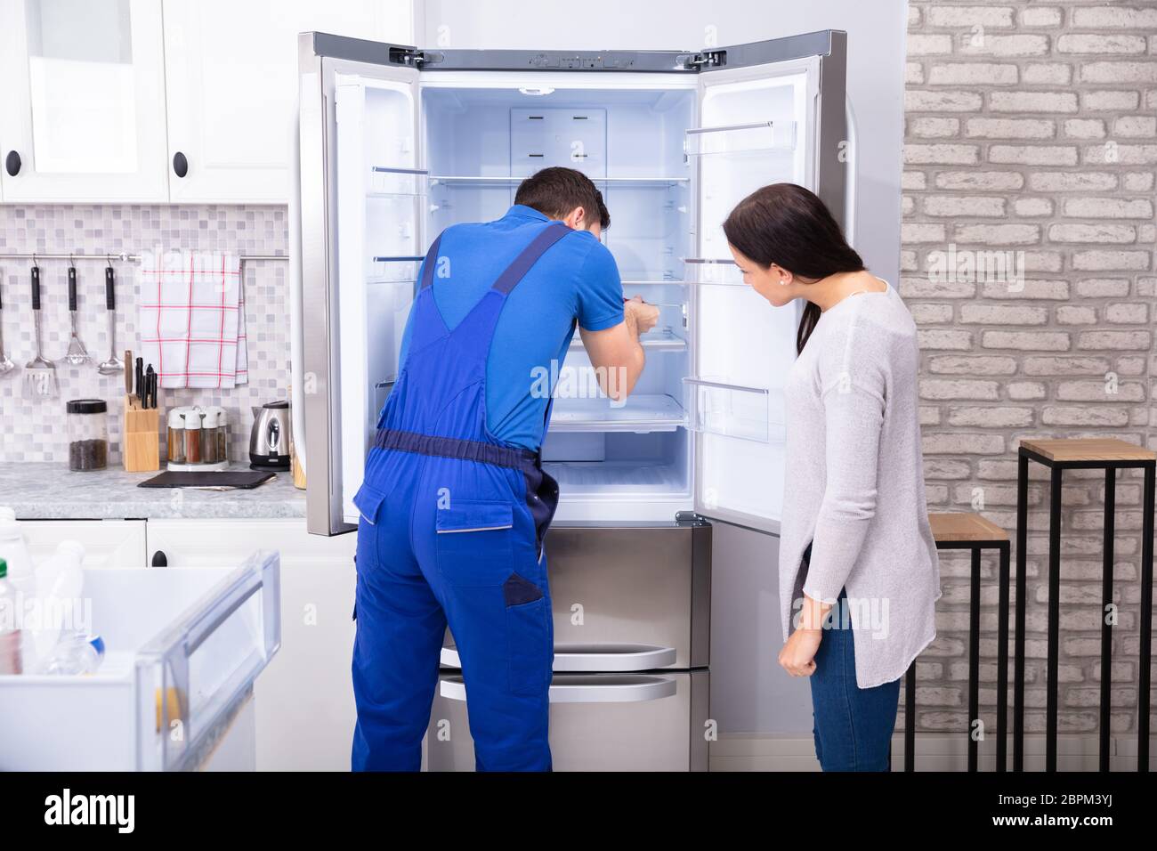 Woman Looking At Male Repairman Fixing Refrigerator With Screwdriver ...