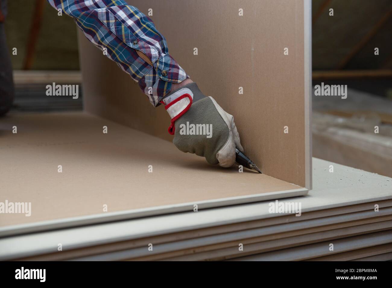Worker cutting drywall plasterboard with construction knife. Attic ...