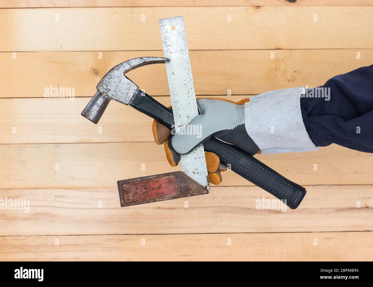 Working hand in glove holding iron ruler and hammer with wall wood ...