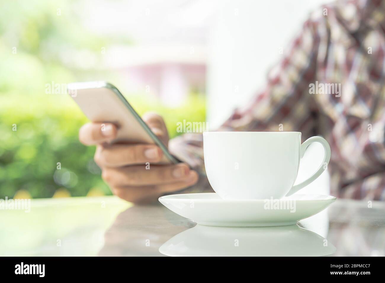 Male hands holding smart phone and cup of coffee on the table outdoor ...