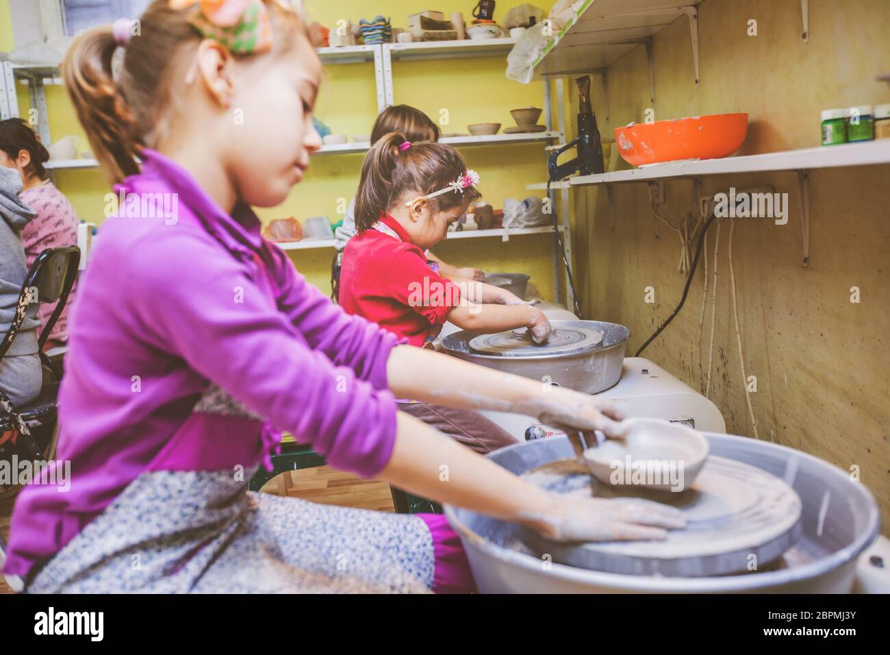 Children molding clay on pottery wheel at art studio learning new skill ...