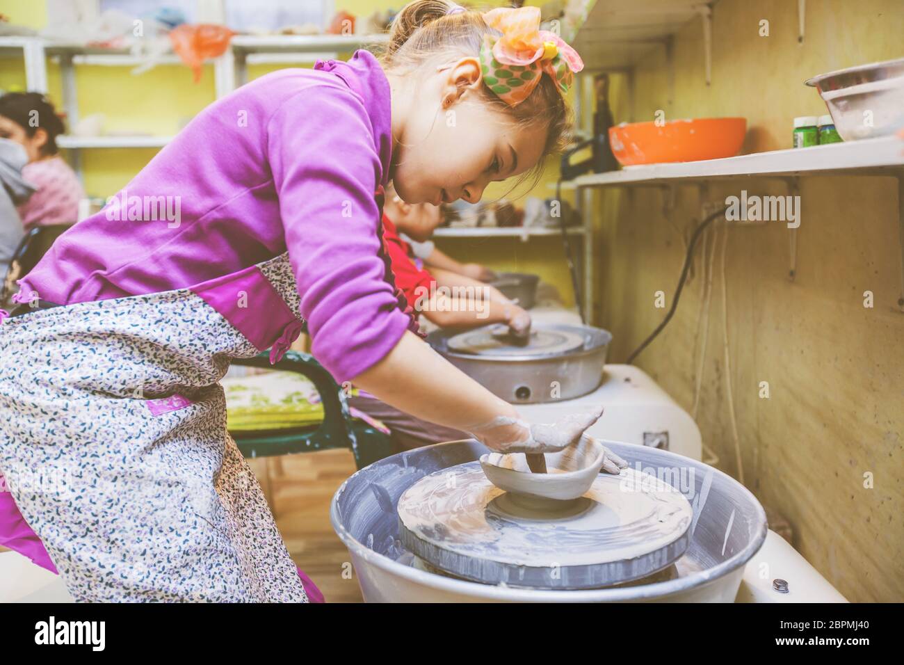 Child molding clay on pottery wheel at art studio learning new skill ...