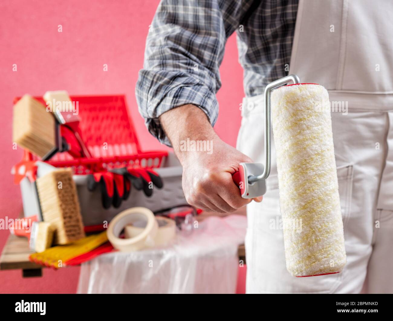 Caucasian house painter worker in white work overalls, with the roller ...