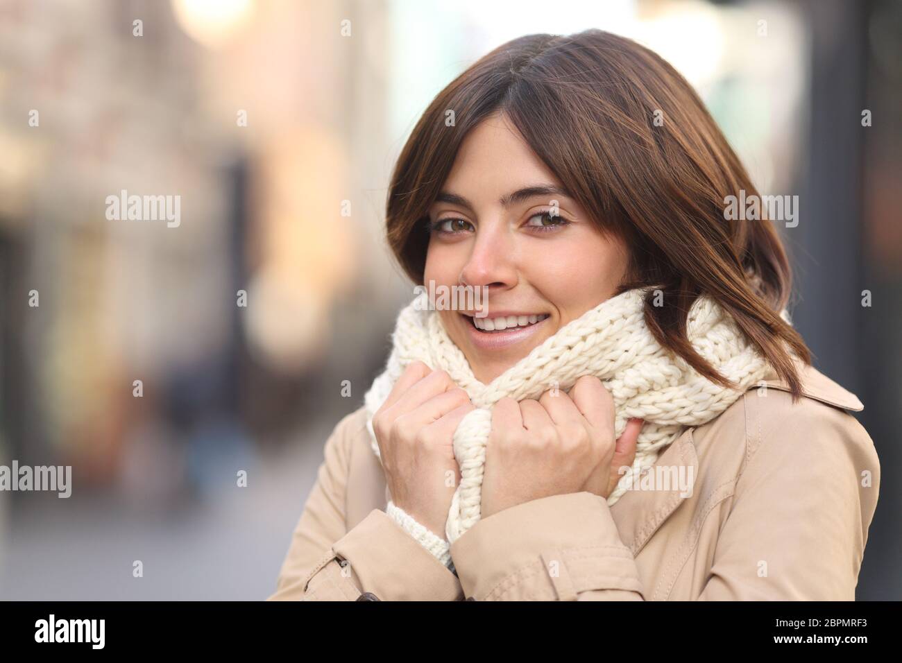 Happy woman being cold grabbing scarg and looking at camera in winter ...