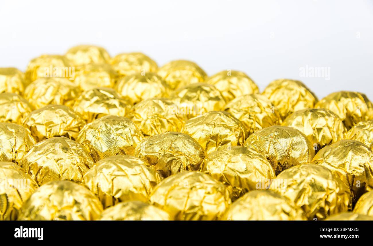 a lot of shiny golden chocolate wrapper in line on white background ...