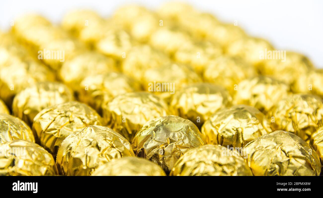a lot of shiny golden chocolate wrapper in line on white background ...